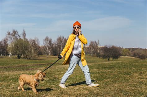 Девушка В Желтой Куртке И Красной Шляпе С Очками Гуляет С Собакойспаниелем В Парке И