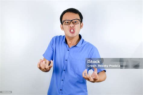 젊은 아시아 남자 입고 파란색 셔츠는 흰색 배경 위에 고립 된 카메라에서 소리지르고 손가락을 가리키는 재미있는 화가 얼굴입니다