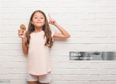 흰색 벽돌 벽 먹는 초콜릿에 젊은 히스패닉 아이 칩 쿠키 생각이 나 질문 넘버 원 행복 한 얼굴로 손가락을 가리키는 놀된 가리키기에 대한 스톡 사진 및 기타 이미지 Istock
