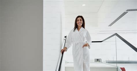 흰색 목욕 가운을 입은 매력적인 여성의 전체 길이 초상화가 미용실의 홀로 향하고 있다 그녀는 카메라를 바라보며 웃고 있다 사진