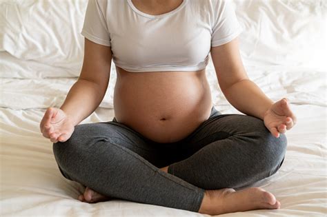 임신 한 여자는 그녀의 아이를 돌보는 동안 집에서 침실에서 침대에 요가 운동을하고있다 임신 한 배에 아기를 들고 행복한 젊은 기대 어머니 출산 전 관리 및 임신 개념에 대한