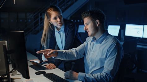 야심 차고 자신감 있는 사업가가 데스크톱 컴퓨터를 사용하며 여성 프로젝트 관리자는 특정 작업 계정 처리 전략적 움직임을 설명합니다 기업 사무실에서 밤에 전문 인력 2명에