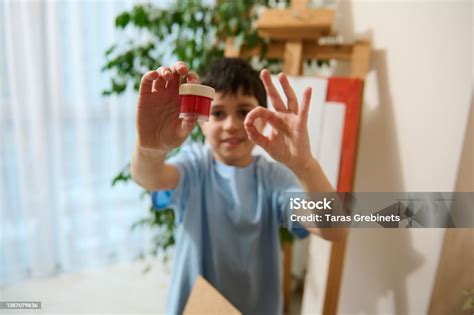 빨간 구아체 페인트를 들고 집에서 나무 이젤에 캔버스에 서 카메라를 보고 Ok 사인을 보여주는 초점 검은 머리 학교 백인 소년 소년 예술가의 손에 초점을 맞춥니다 8 9