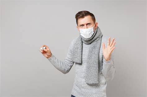 스웨터 스카프 무 균 얼굴 마스크 홀드 온도계 회색 배경에 고립 손을 확산 충격 젊은 남자 건강 한 라이프 스타일 아픈 질병
