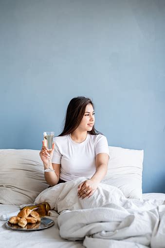 젊은 갈색 머리 여자 앉아 침대에 깨어 있는 빨간 마음 모양풍선 과 장식 마시는 샴페인 먹는 크루아상 앉음에 대한 스톡 사진 및 기타 이미지 Istock