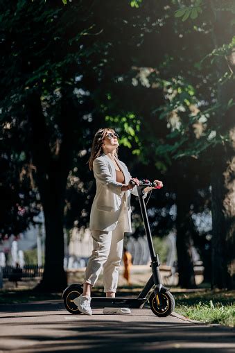 선글라스와 흰 양복을 입은 아름다운 젊은 여성이 도시 공원에서 전기 스쿠터와 함께 서 있습니다 개에 대한 스톡 사진 및 기타 이미지 Istock