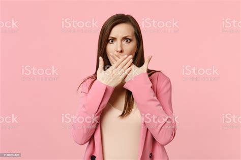 충격 자극 된 젊은 여자의 초상화 카메라를 보고 재킷을 입고 파스텔 핑크 배경에 고립 된 손으로 입을 덮고 사람들은 진심으로 감정 라이프 스타일 개념입니다 복사 공간을 모의