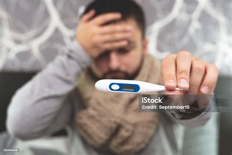 질병 집에서 응원하십시오 한 청남이 아프고 집에서 치료를 받습니다 체온 측정 사람의 손에전자 온도계입니다 모의 고개 감염 전염병 간균 운반대 감기와 독감에 대한 스톡 사진