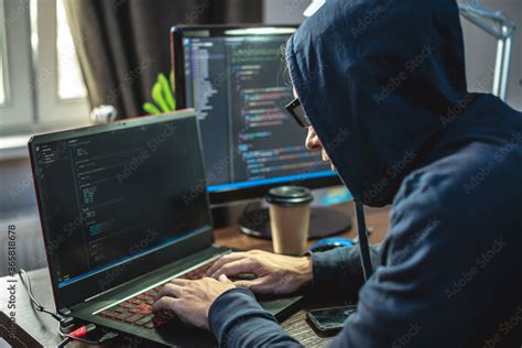 Hacker In The Hood Is Programming Virus Code At The Keyboard For The Laptop Internet Fraud And