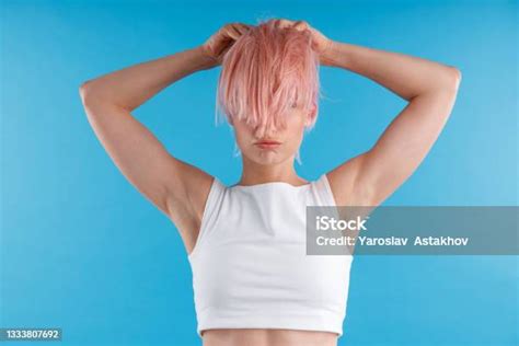 흰색 셔츠를 입은 젊은 여성이 매끄러운 스트레이트 핑크 헤어 포니 테일로 놀고 파란색 스튜디오 배경에서 고립 된 포즈를 취하면서 그녀의 얼굴을 뒤에 숨깁니다 30 34세에