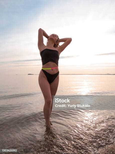 해수면에 태양의 길을 반사하는 바다 파도의 배경에 대해 일몰에 검은 수영복을 입은 젊은 검은 머리 의 날씬한 여성 20 24세에 대한 스톡 사진 및 기타 이미지 Istock