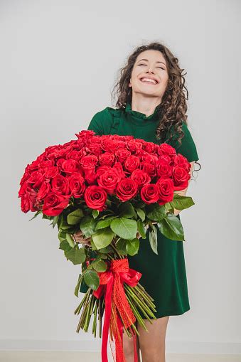 긴 물결 모양의 머리를 가진 쾌활한 젊은 아가씨는 흰색 배경 위에 고립 된 여성의 날에 빨간 장미 꽃다발을 얻을 흥분됩니다 갈색 머리에 대한 스톡 사진 및 기타 이미지