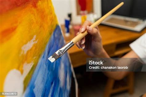 암실의 따뜻한 빛에서 여자 손 예술가를 클로즈업하고 브러시와 변형 아크릴 색상으로 그림을 그립니다 크리에이티브 스튜디오에서 예술