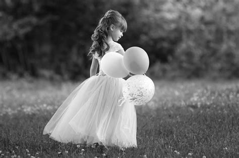 검은 색과 흰색 프로필 흐린 배경에 피는 필드에 서 공기 풍선 긴 흰색 드레스꽤 작은 금발 긴 머리 소녀의 전체 길이 초상화 행복 한 어린 시절 개념입니다 감정에 대한 스톡