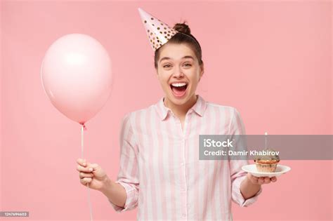 생일 모자를 쓰고 풍선과 접시를 케이크로 들고 행복하고 놀라움에 만족하며 분홍색 배경에 고립 된 어린 흥분 한 십대 소녀 여자에 대한 스톡 사진 및 기타 이미지 Istock