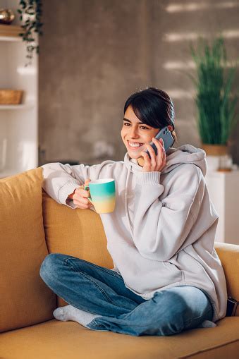 스마트폰을 사용하고 집에서 소파에서 커피를 마시는 아름다운 여자 25 29세에 대한 스톡 사진 및 기타 이미지 25 29세