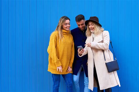 거리에서 함께 즐거운 시간을 보내는 행복한 친구 두 여성과 한 남자 미소와 웃음 자화상과 파란색 배경에 휴대 전화를 사용하여 우정과 라이프 스타일의 개념 스마트폰에 대한