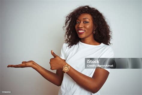 고립 된 흰색 배경 위에 서있는 티셔츠를 입은 젊은 아프리카 계 미국인 여성은 손바닥 손을 표시하고 엄지 손가락으로 확인 제스처를하고 행복하고 쾌활한 미소를 지었습니다 T