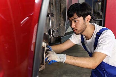 남자 기술자 자동차 정비사는 제복을 입고 수리 차고 역에서 리프트 자동차 서비스를 점검하거나 유지 보수합니다 렌치를 잡고