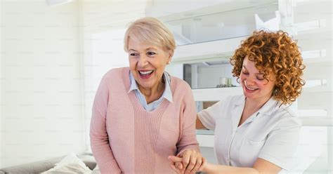 웃는 간호사가 노인 여성이 요양원을 돌아다니는 것을 돕고 있습니다 행복한 여성 간병인과 집에서 함께 걷는 노인 여성의 초상화 노인 여성을 돌보는 전문 간병인 사진