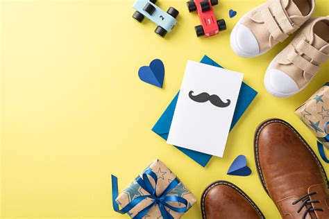 아기는 아빠와 함께 아버지의 날을 축하합니다 아버지의 드레스 슈즈 아기의 운동화 하트 콧수염이 있는 엽서 텍스트나 광고를 위한 공간이 있는 노란색 배경의 선물 상자를