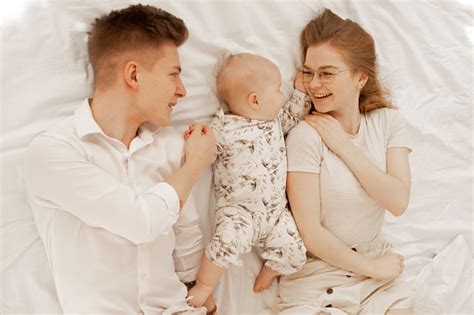 젊은 어머니와 아버지는 침대에 작은 아기와 함께 누워 재미 있고 흰색 배경에서 즐겁습니다 부모와 유아 사이의 귀여운 관계 무료 복사 공간 행복한 가족과 부모의 애정 20