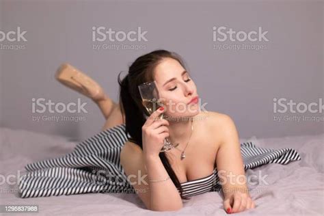 회색 침실의 침대에 샴페인 한 잔과 저녁 칵테일 드레스에 행복한 매력적인 갈색 머리 여자 애프터 파티 외로움 20 29세에 대한