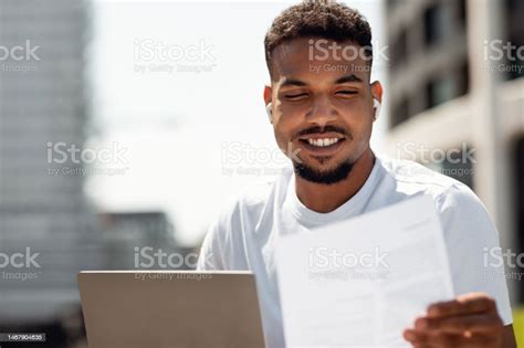 야외에서 문서와 노트북 컴퓨터로 일하는 행복한 흑인 도시 지역에 앉아 Pc를 사용하여 보고서 준비 20 24세에 대한 스톡 사진