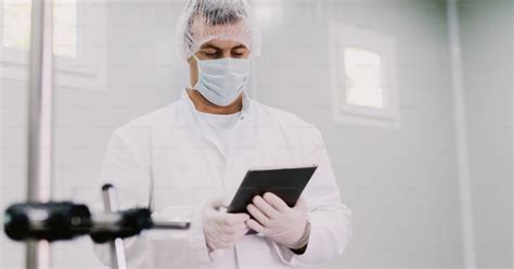 태블릿을 사용하여 멸균 옷을 입은 젊은 남자의 사진 공장에서 생산 라인 제어 생산 라인에 화장품을 가진 병 사진 Unsplash의 매니저 이미지