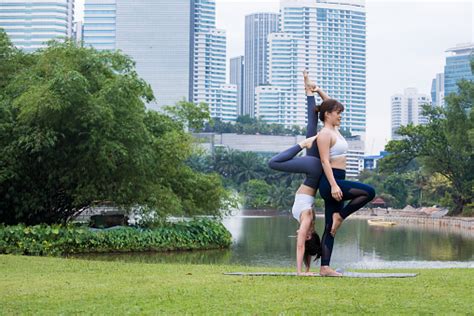 높은 결단력과 힘을 가진 두 명의 젊은 활기찬 아시아 여성은 아침에 도시 경관에 맞서 자연 공원에서 아크로요가 연습하고 스트레칭 운동을 합니다 25 29세에 대한 스톡 사진