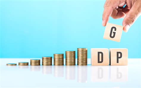 Gdp라고 적힌 나무 블록을 들고 있는 손과 탁자 위에 놓인 동전 뭉치 경제 성장을 상징하며 금융 번영을 측정하는 데 있어 국내총생산의 역할을 강조합니다 개발에 대한 스톡