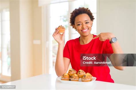 젊은 아프리카 계 미국인 여자 먹는 초콜릿 칩 머핀 와 깜짝 얼굴 가리키는 손가락 에 자신 가리키기에 대한 스톡 사진 및 기타 이미지 가리키기 가정 생활 개념