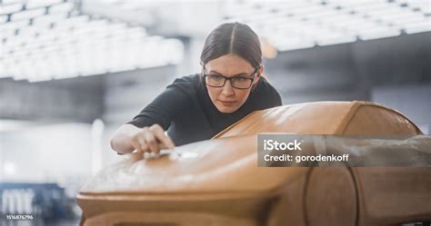 새로운 생산 자동차의 3d 점토 모델을 조각하는 여성 자동차 디자이너의 초상화 프로토타입 컨셉 차량의 표면을 조심스럽게 다듬기 위해 주걱을 사용하는 젊은 여성 3차원 형태에