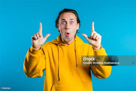 파란색 스튜디오 배경에 손가락을 가리키는 아이디어 순간을 갖는 노란색으로 남자를 숙고 하는 젊은 생각의 초상화 유레카 제스처를 보여주는 행복한 학생 남자 미소 긍정적인 감정