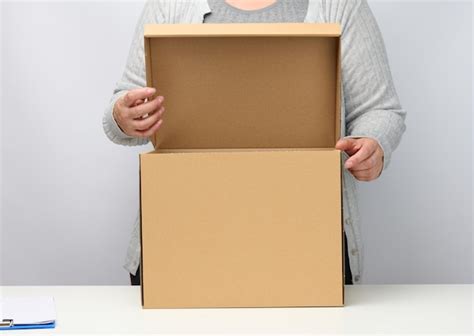 Premium Photo Woman In Gray Clothes Stands And Holds Open Brown Box On A White Background Moving
