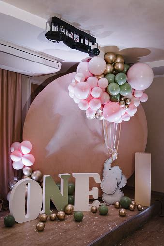 아치는 분홍색 황금색 녹색 풍선 종이 장식 코끼리 색종이로 장식되어 있습니다 1살짜리 소녀 또는 소년을 위한 생일 파티는 배경 갈색 사진 벽에 있습니다 리셉션 축하