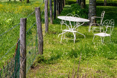 나무 기둥과 철조망 울타리 옆에 있는 푸른 잔디 위에 테이블과 금속 의자 세 개가 있습니다 0명에 대한 스톡 사진 및 기타
