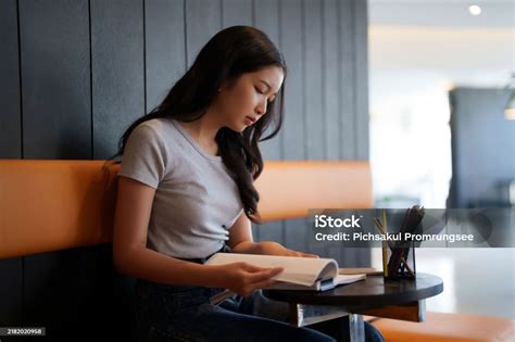 책을 읽고 책에서 정보를 쓰는 아시아 청소년 여성은 카페에서 공부하고 교육 지식에 대해 배우면서 시험 시험을 준비하기 위한 과제 숙제를 합니다 20 24세에 대한 스톡 사진