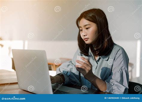 Asian Woman Wearing A Blue Striped Shirt Sitting In Front Of A Laptop
