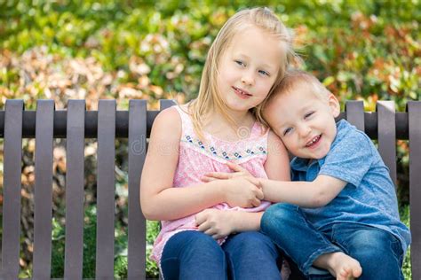 Große Schwester Und Kleiner Bruder Hugging On Eine Bank Am Park