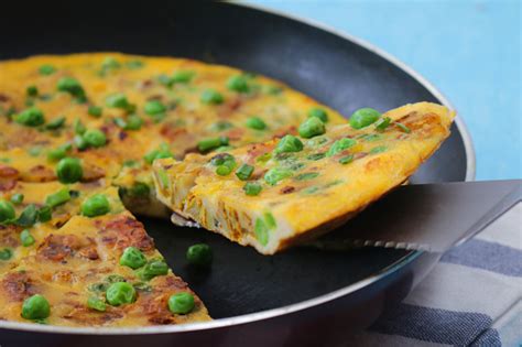 녹색 완두콩 장식이 없는 스페인 토르티야 프리타타의 삼각형 슬라이스의 클로즈업 이미지 파란색과 흰색 박탈 된 차 수건 옆에 집에서 만든 스페인 아침 식사 오믈렛 전경에