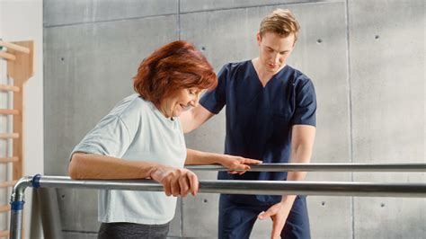 다리 부상을 입은 강한 중년의 초상화는 평행 한 막대를 들고 성공적으로 걷습니다 전문 물리 치료사는 장애인이 재활 물리 치료를하도록 돕고 돕고 훈련시킵니다 물리치료에 대한
