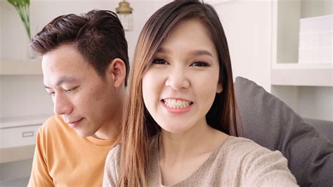 아시아 커플 스마트폰 영상 통화를 사용 하 여 친구와 함께 집에서 거실 달콤한 부부는 집에서 편안 하 게 소파에 누워 있는 동안