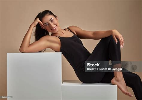 운동복을 입은 젊은 여자가 갈색 배경 앞에 하얀 상자에 앉아 있다 인체에 대한 스톡 사진 및 기타 이미지 인체 20 29세 건강한 생활방식 Istock