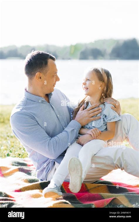 A Little Daughter Is Sitting On Her Fathers Lap On A Blanket In The