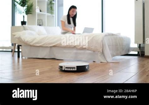 Young Asian Woman In Bedroom Controlling Robot Vacuum Cleaner Concept Of Automated Cleaning