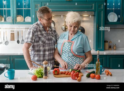 Old Husband Watching At Wife Cooking A Salad For A Breakfast And