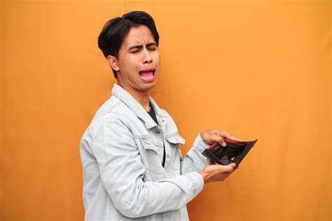 가난한 아시아 남자가 빈 지갑을 들고 포즈를 취하고 빈 지갑을 들고 슬픈 얼굴로 옆을 바라보며 포즈를 취하는 아시아 남자는