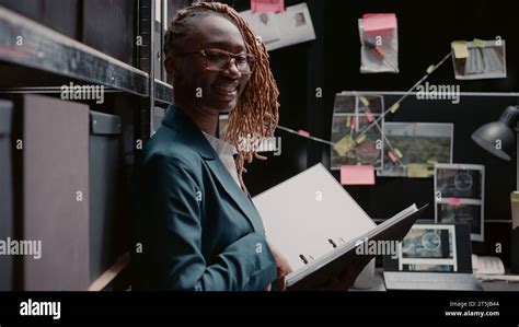 Female Police Officer Reading Case Information In File Standing In Incident Room Private