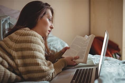 Free Photo Woman Reading A Book And Using Laptop On Bed